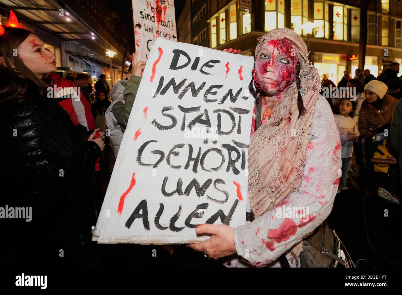 A woman dressed up in a scary costume holds a sign reading "The city ...