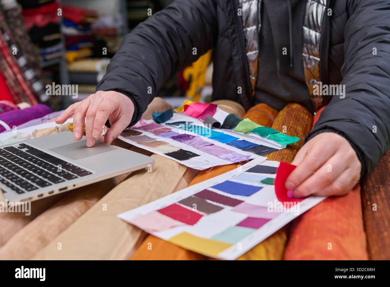 Fashion designer working with fabric swatches and laptop, selecting ...