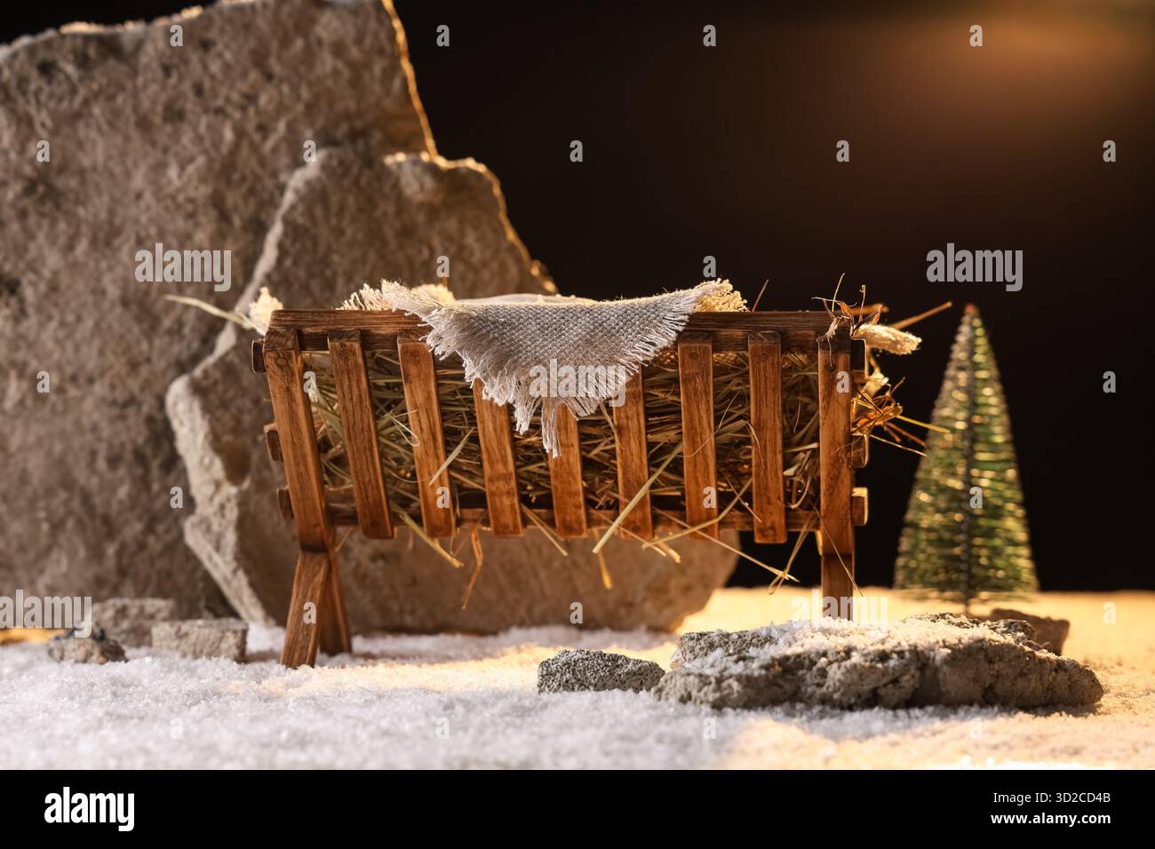 Manger with baby Jesus, rocks and Christmas tree on snow against dark ...