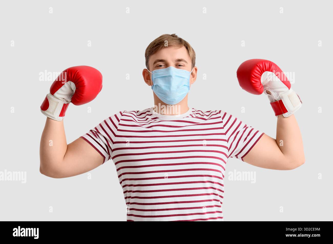 Young man in medical mask and boxing gloves showing muscles on white ...
