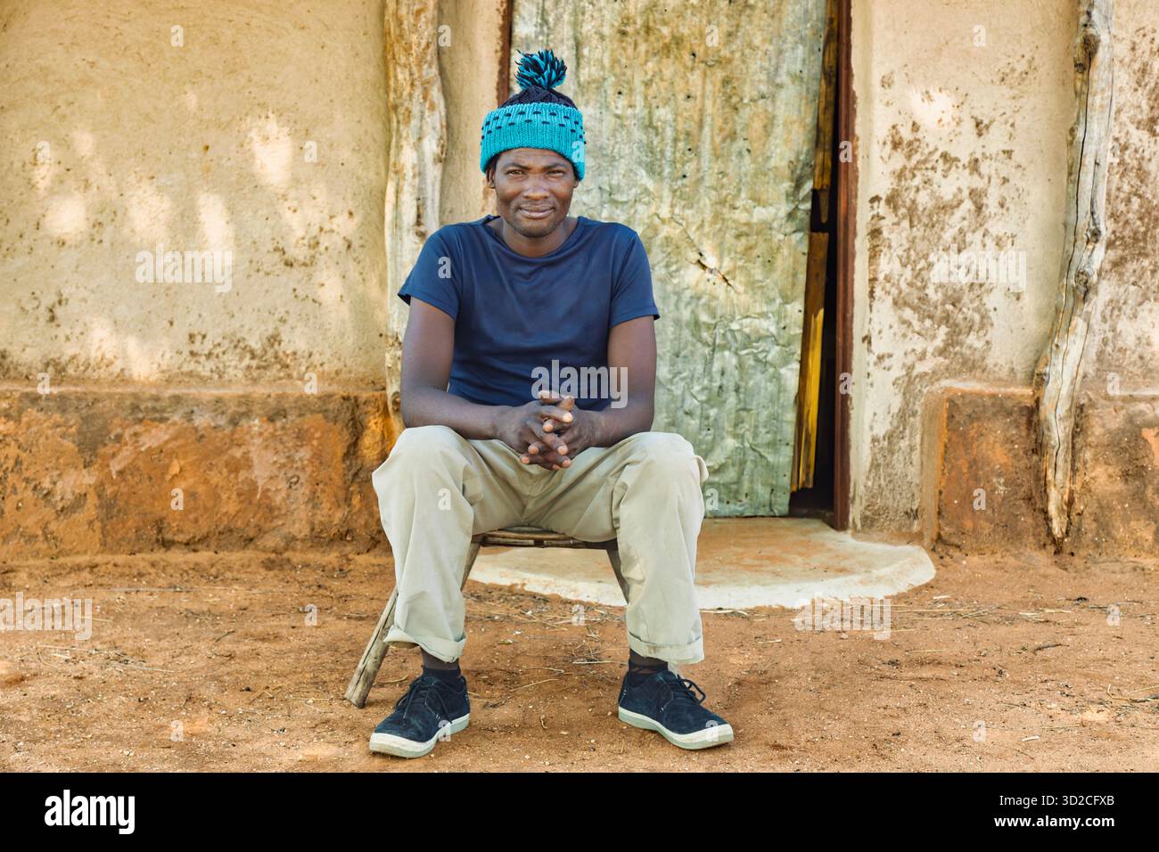 single african man, village life, sited on a chair in the yard, in ...