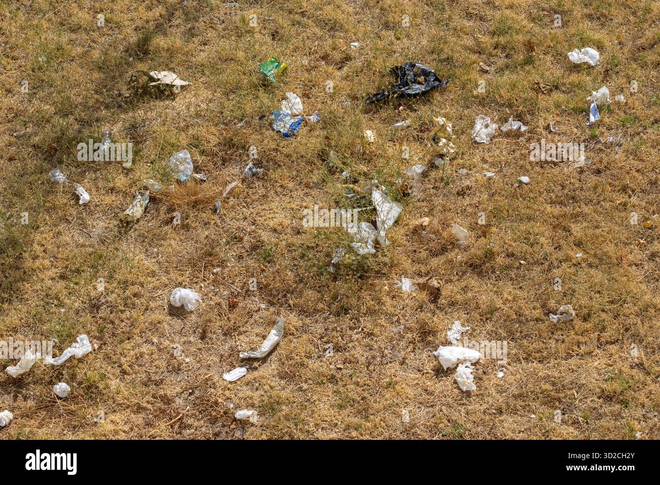 Plastic waste and garbage scatter across dry grass, showing ...