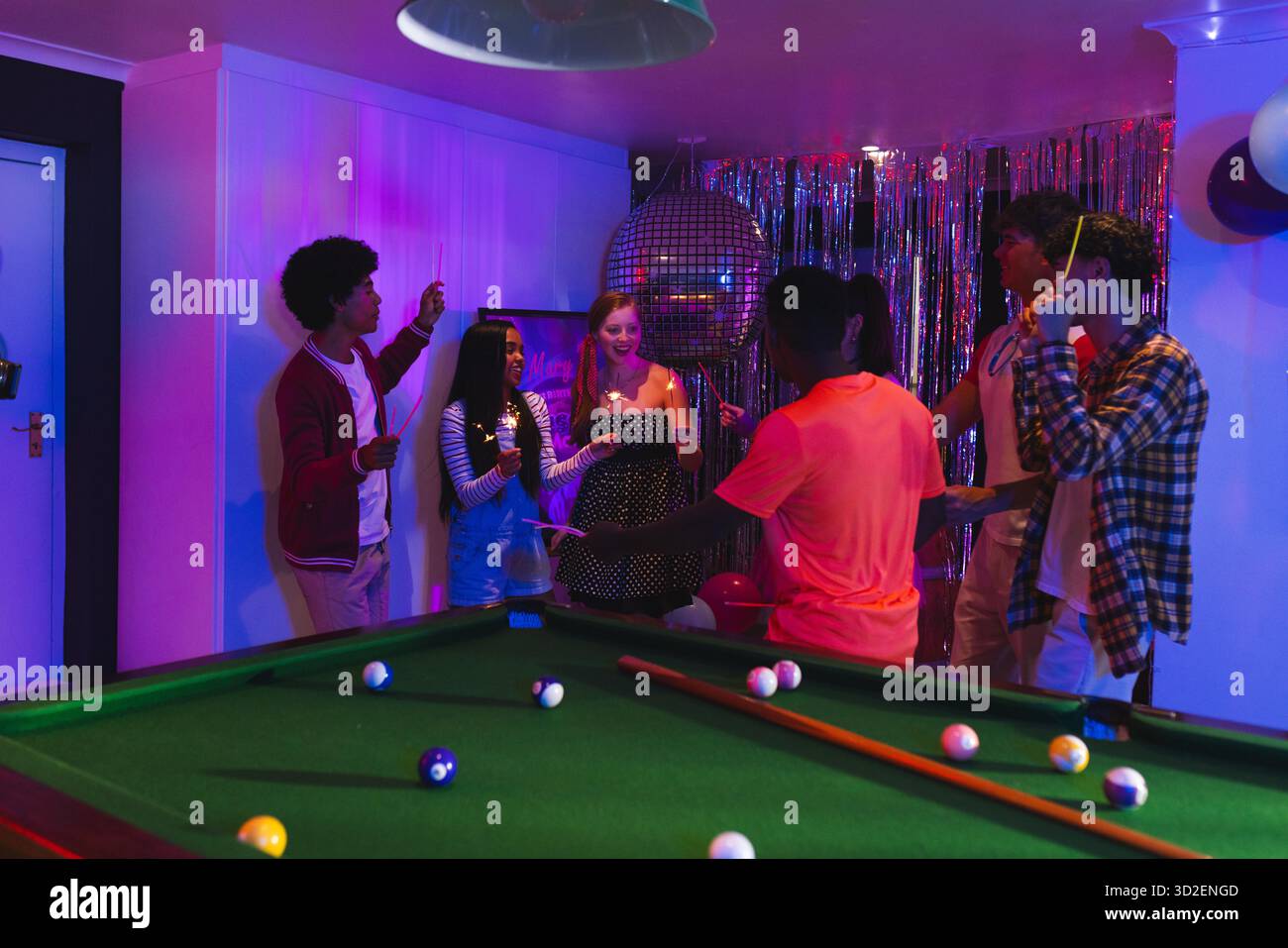 Teenagers celebrating around pool table with colorful lights and ...