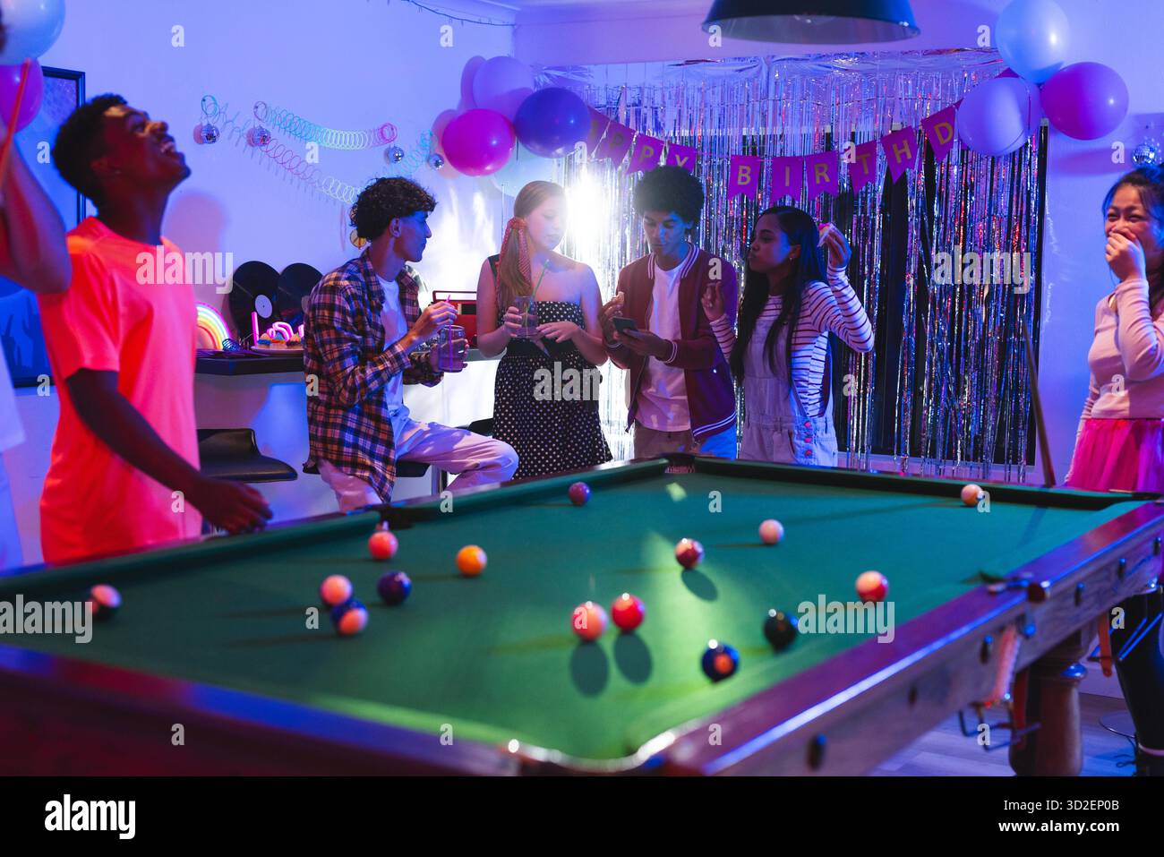 Teens celebrating birthday around pool table with balloons and ...