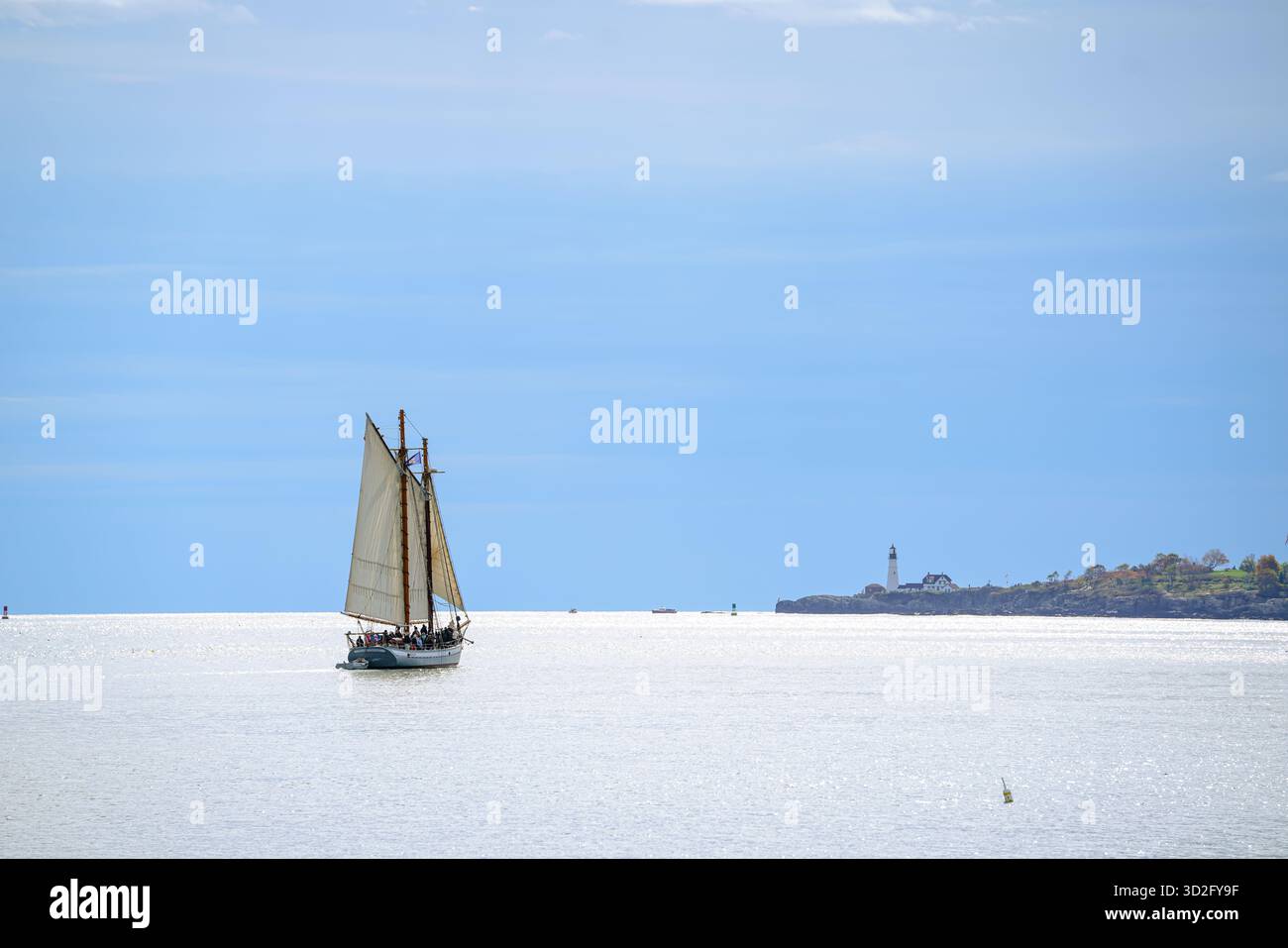 A schooner sails toward the lighthouse on a bright day shimmering light ...