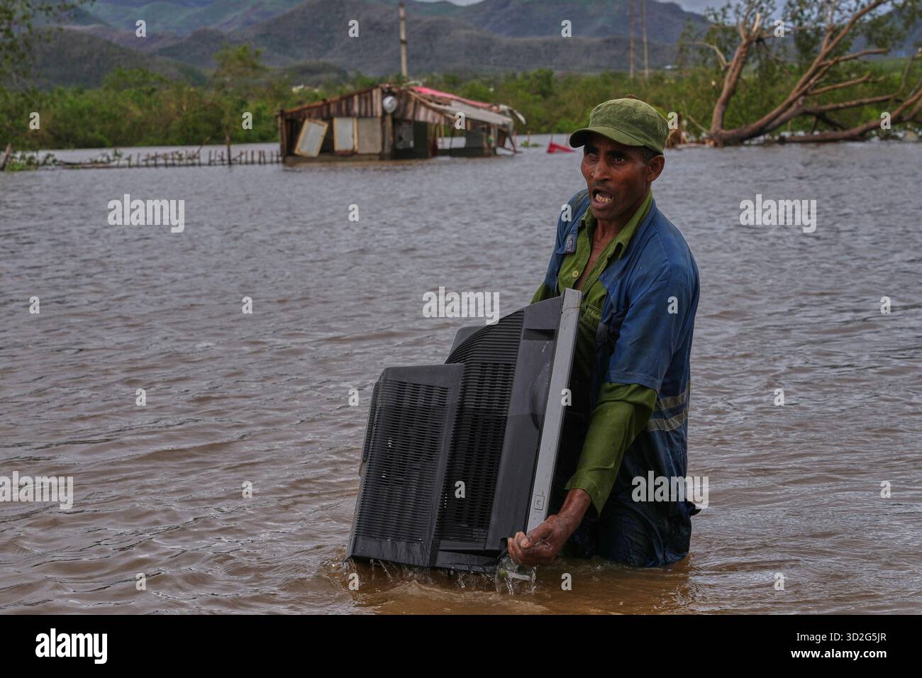 FILE - A man wades through a flooded area carrying a TV from his home ...