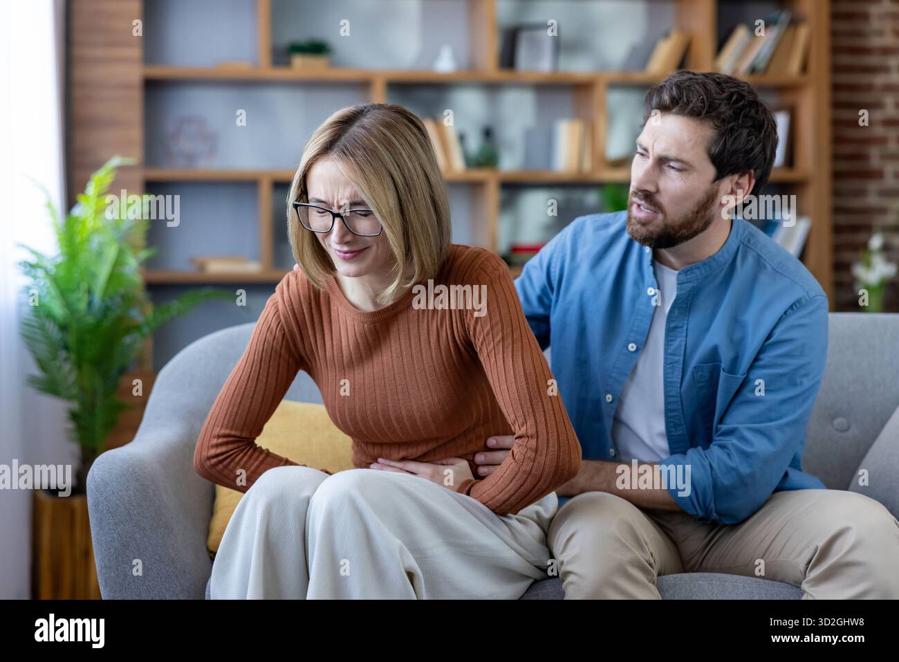 Woman feeling severe abdominal pain or cramps while sitting on a sofa ...