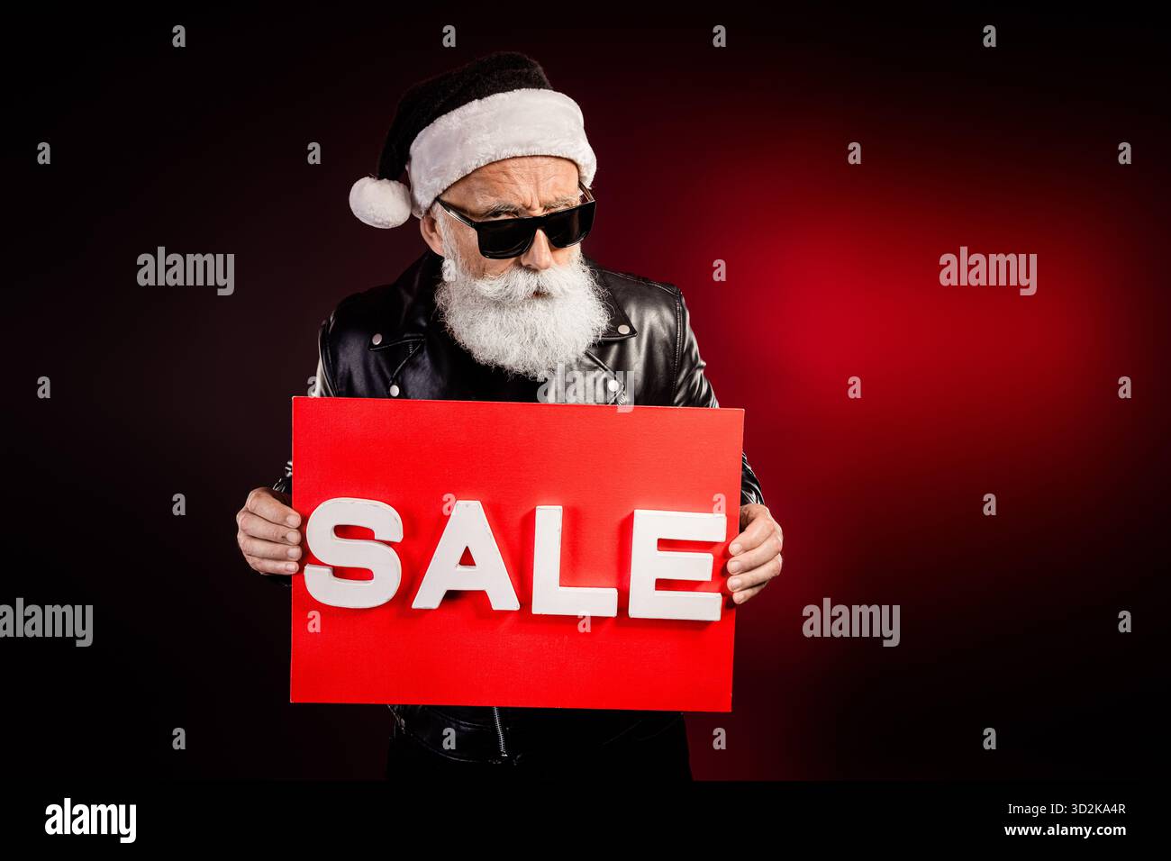 Santa rocker in leather jacket holds a bold red sale sign in a moody ...