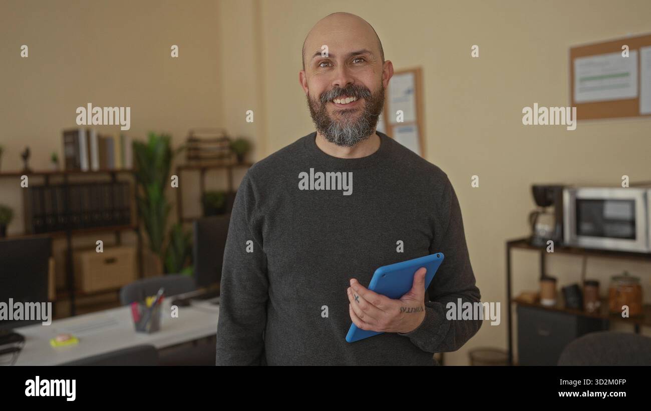Bald man with beard holding tablet in modern office with plants and ...