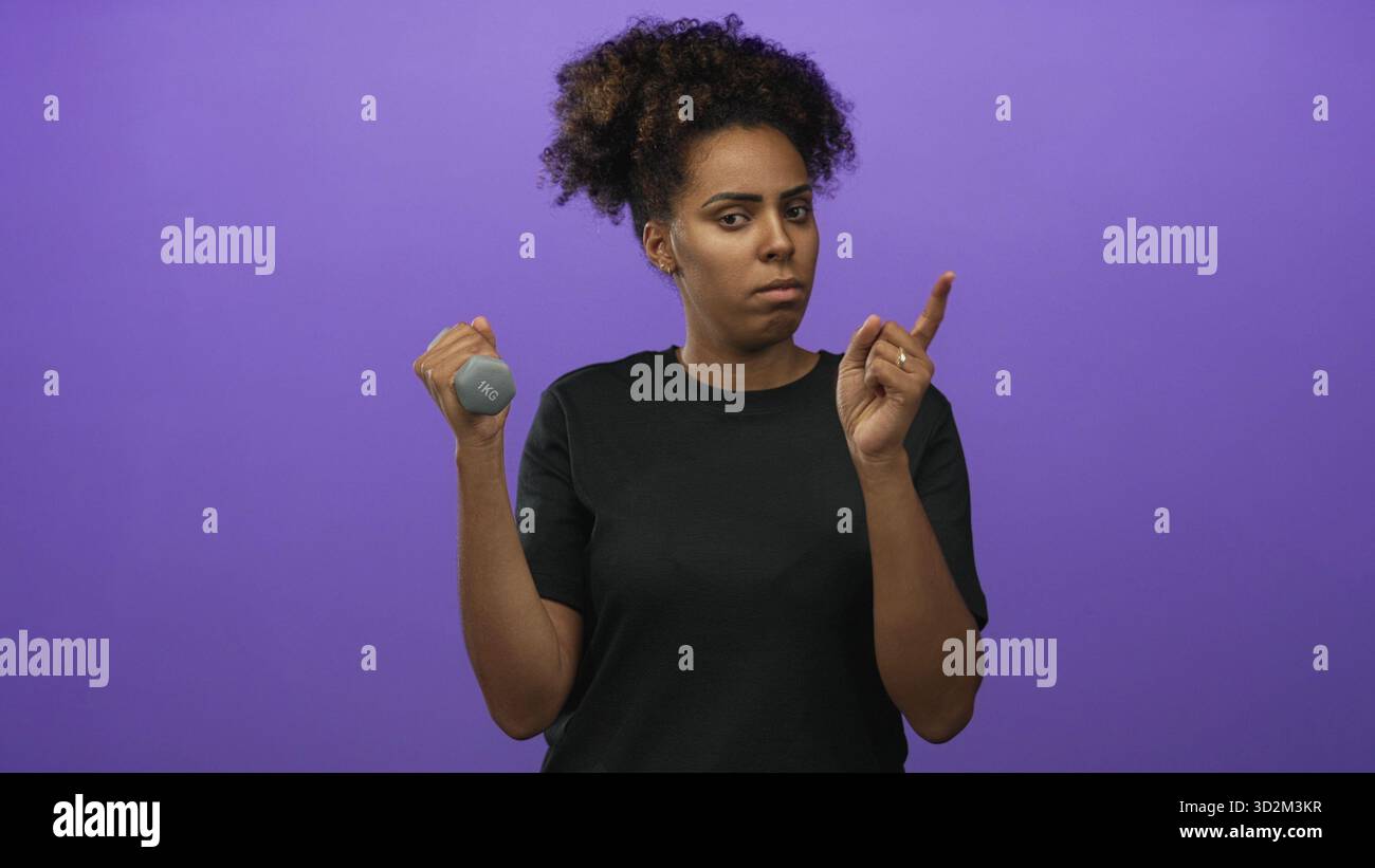 Woman holding 1kg dumbbell and pointing finger at weight in studio ...