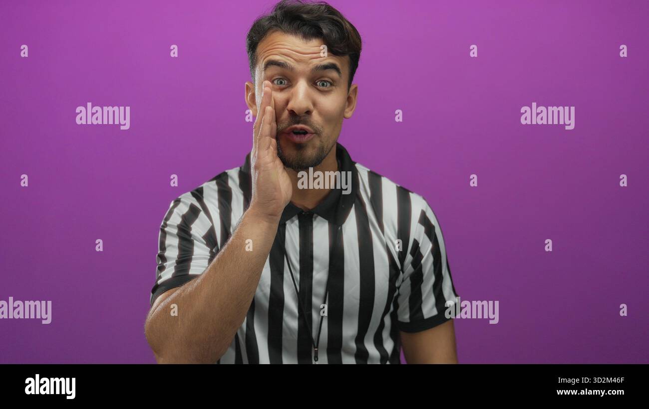 Young hispanic male referee gestures and shouts against a vibrant pink ...