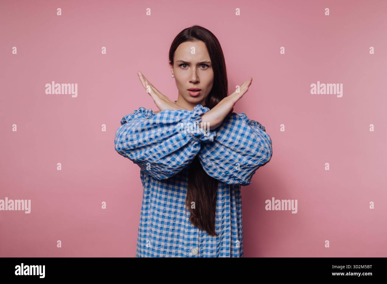 Woman in blue checkered shirt making an X with arms against pink ...