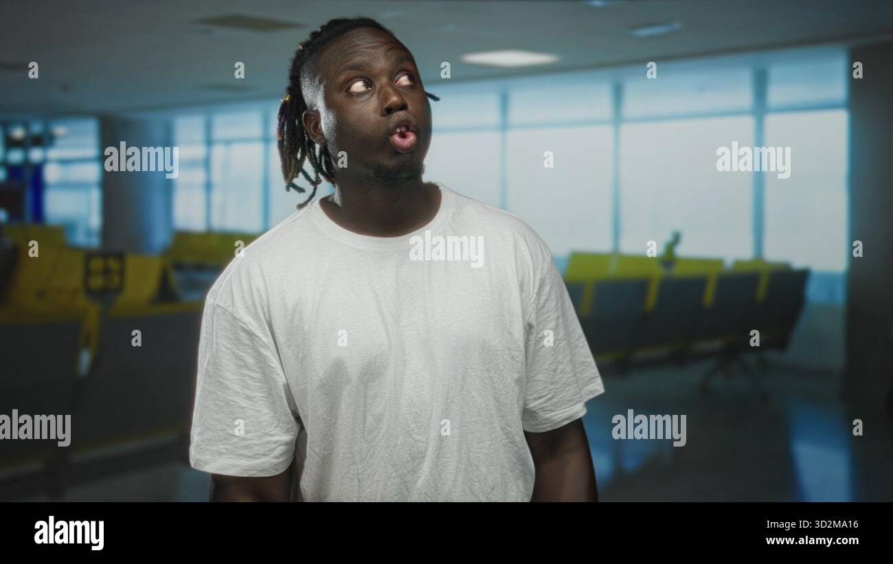 Man with pucker mouth looking up in airport terminal wearing white ...