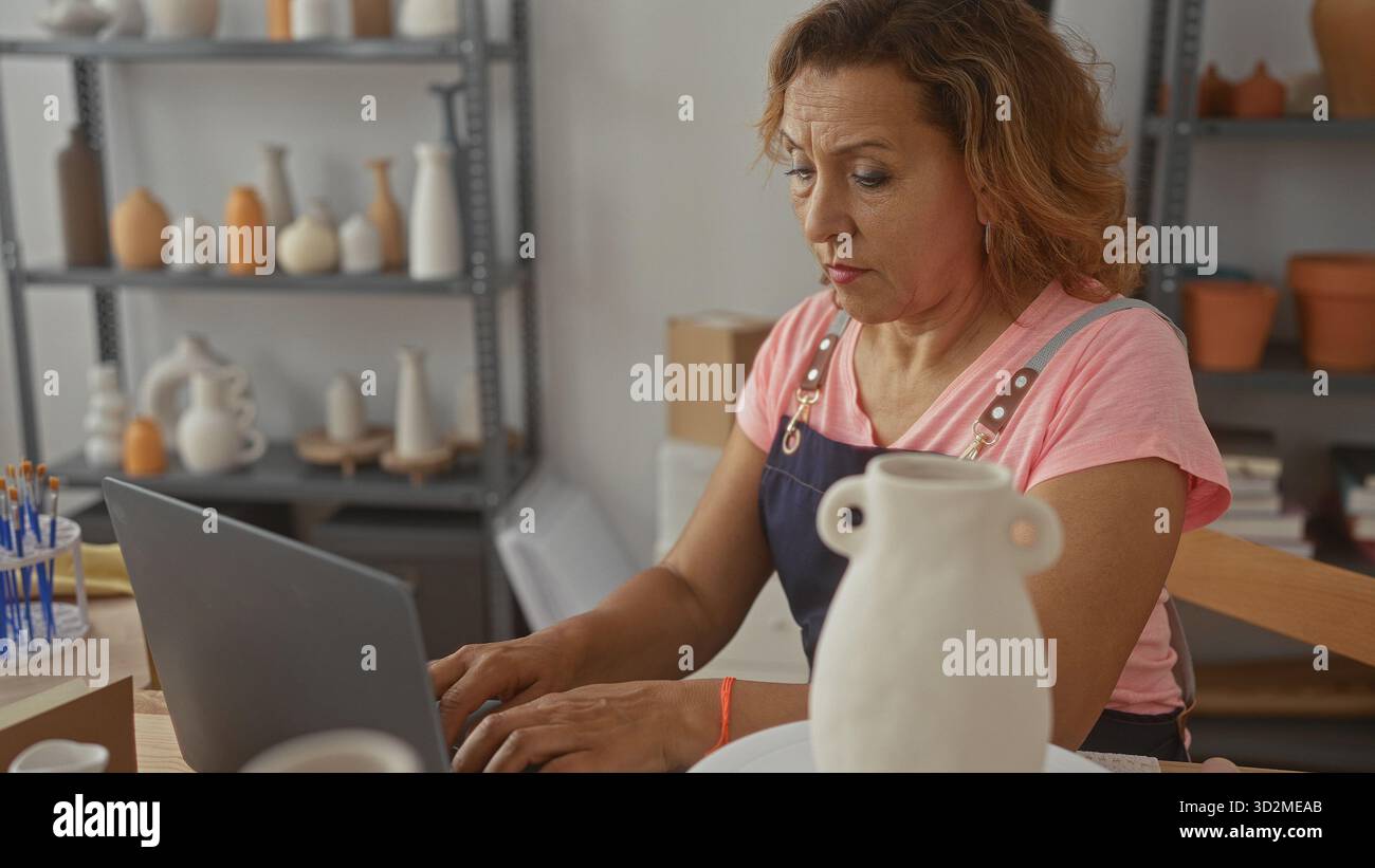 Artisan woman types on laptop beside handmade pottery vase and ceramic ...