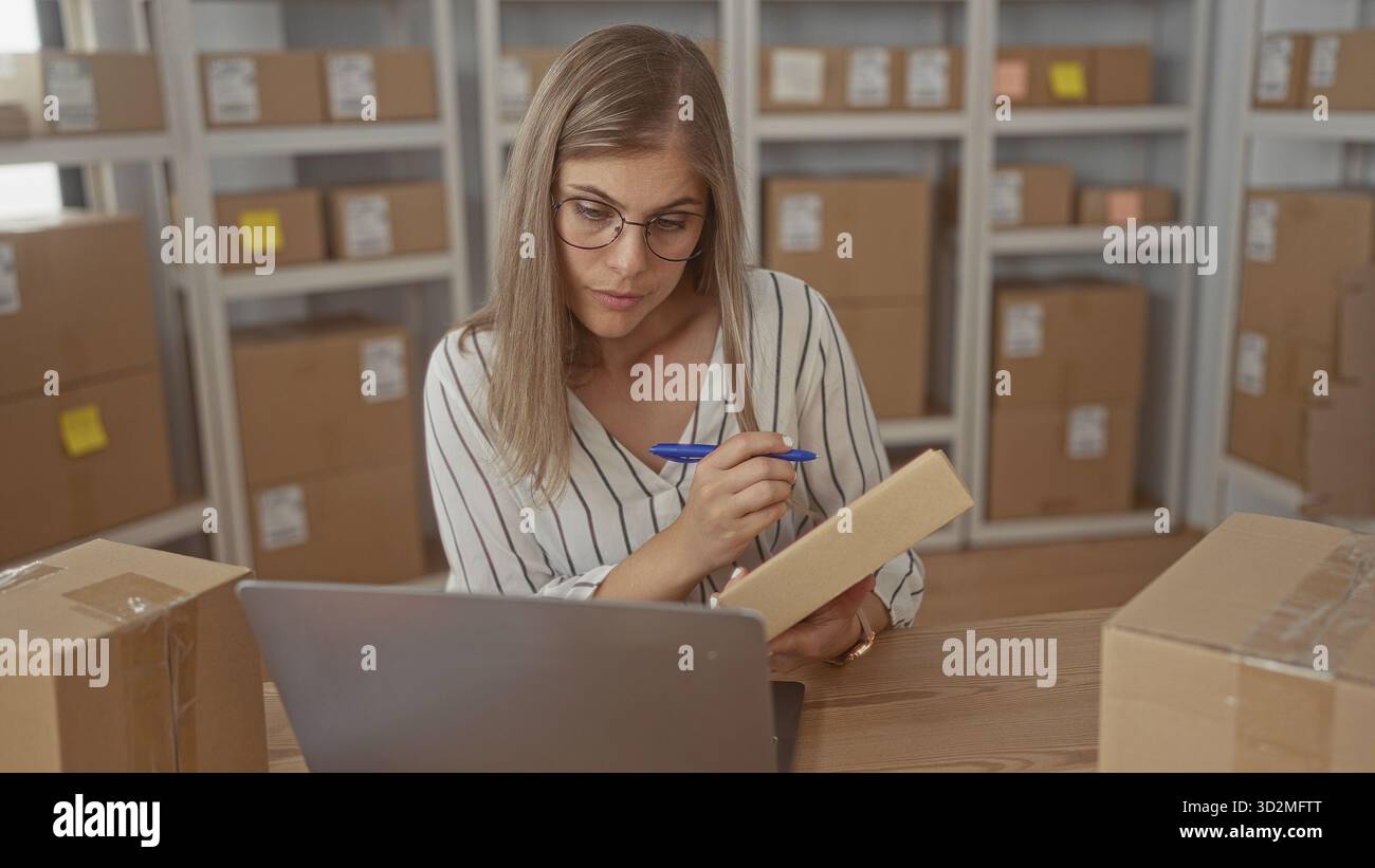 Blonde woman writing on parcel at a desk beside laptop with shelves of ...