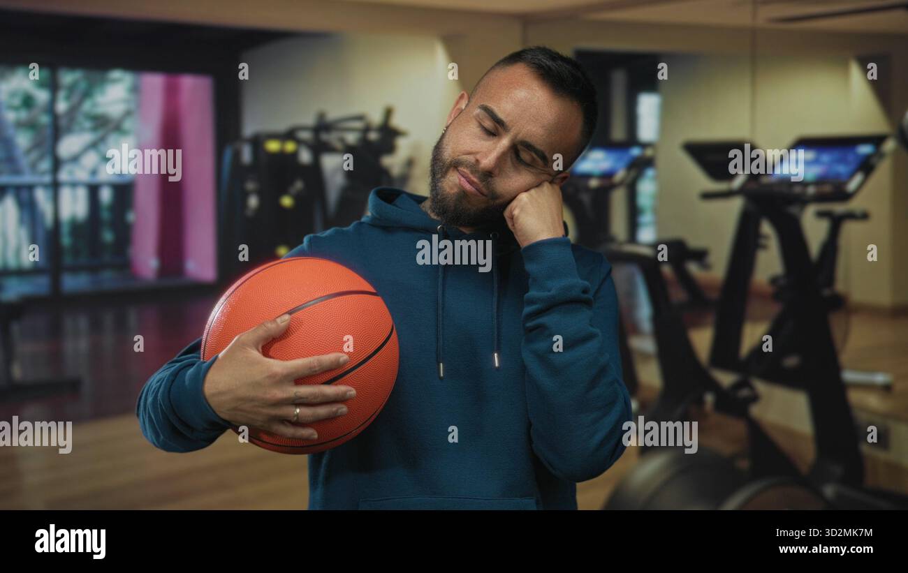 Man holding basketball against chest with hands and closed eyes in gym ...