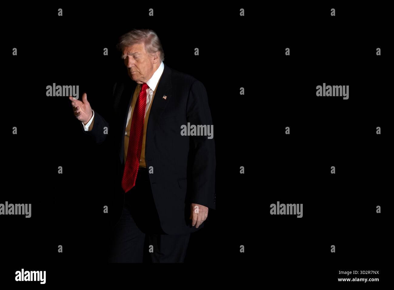 President Donald Trump is illuminated by a camera flash as he walks ...