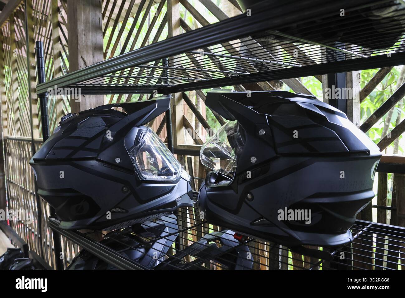 Two dark grey motorcycle helmets sit side by side on shelf, ready for ...