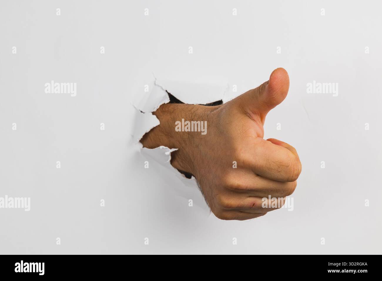 A hand emerges from a torn section of a white wall, displaying a thumbs ...