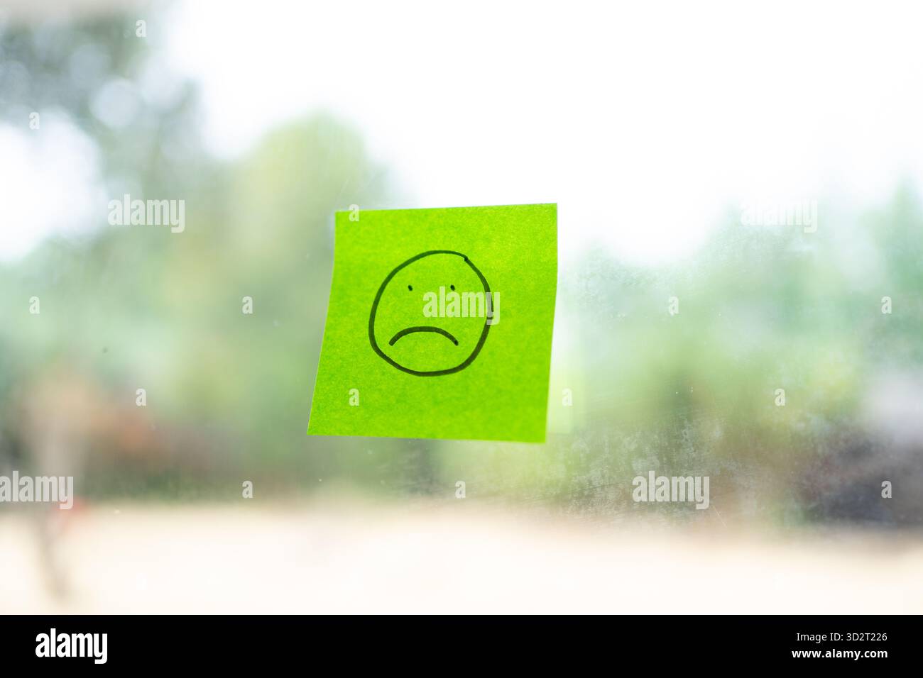 Green sticky note with a drawn sad face adhered to a transparent window ...