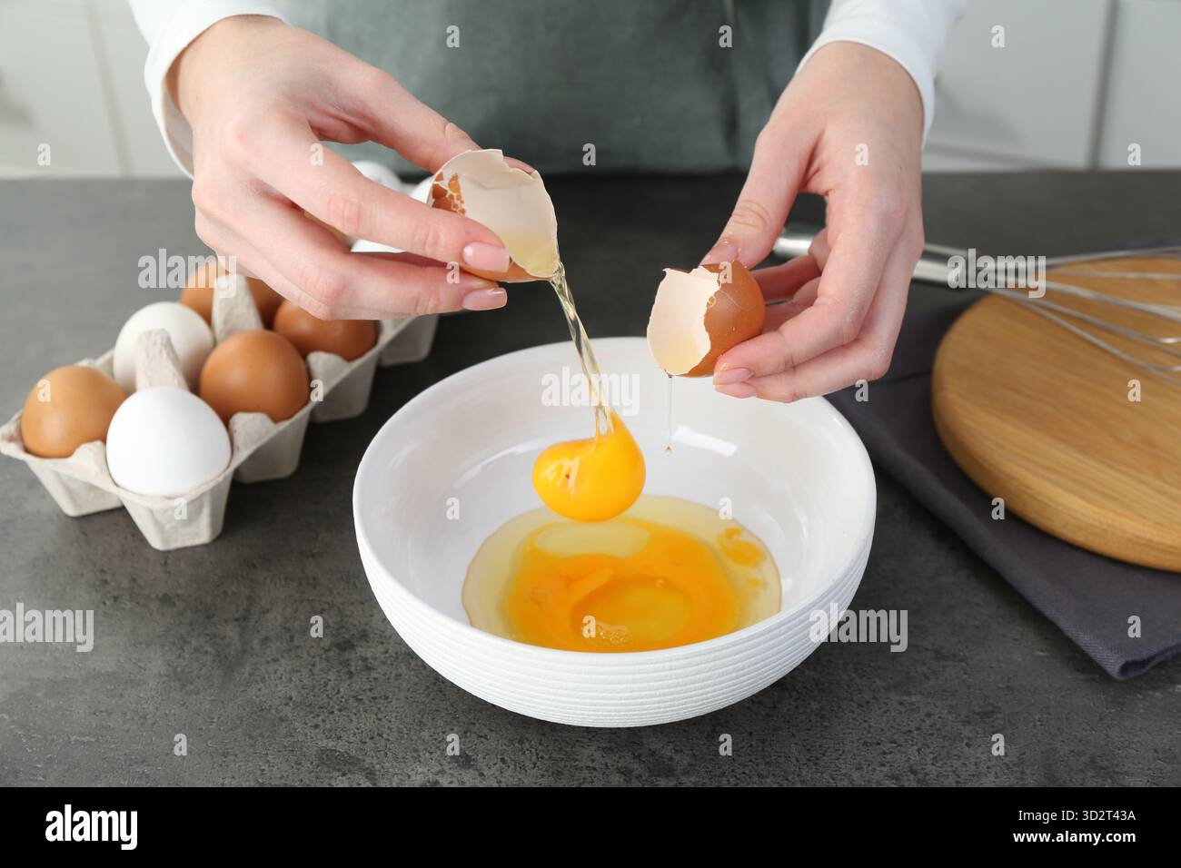 Woman cracking egg into bowl at grey table in kitchen, closeup Stock ...