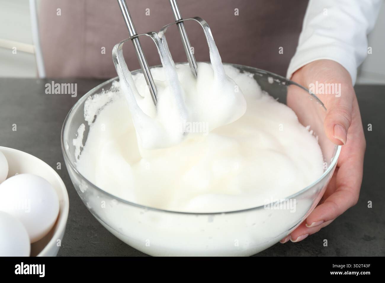 Woman beating egg whites with mixer at grey table in kitchen, closeup ...