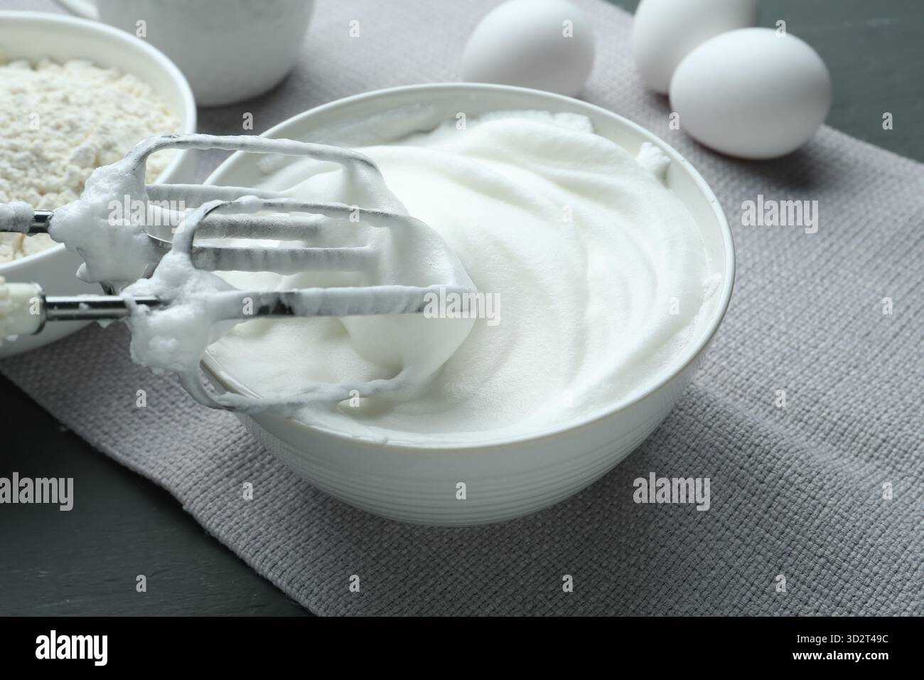 Whipped whites in bowl, mixer, flour and eggs on grey wooden table ...