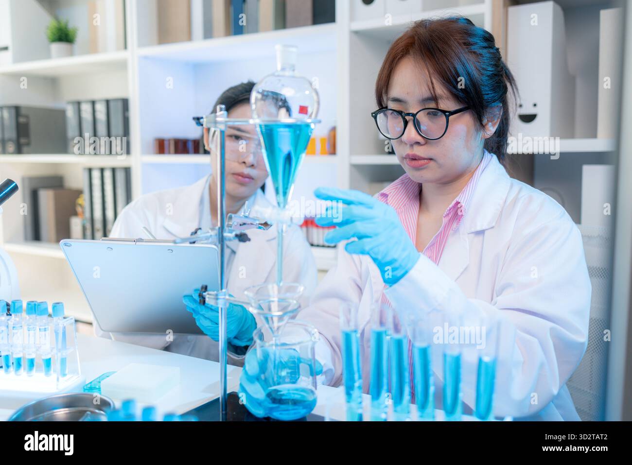 Two chemists in white lab coats working together in a modern laboratory ...