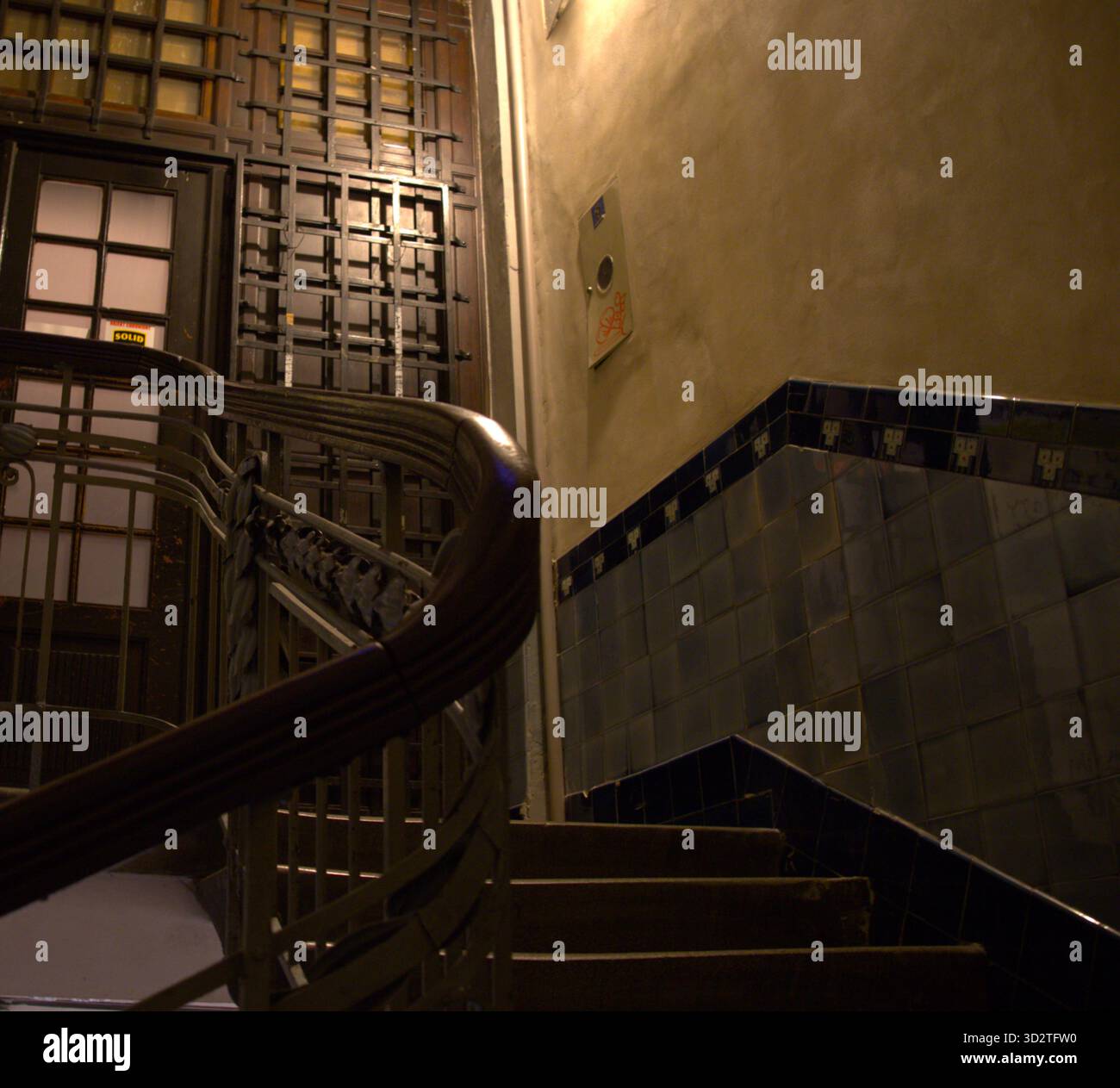 A dimly lit stairwell rises past a curved wooden banister and ornate ...
