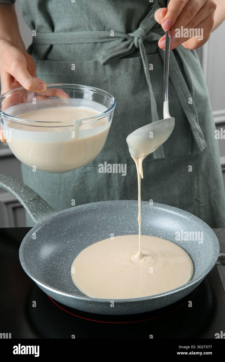 Woman pouring liquid dough from bowl into frying pan at grey table in ...