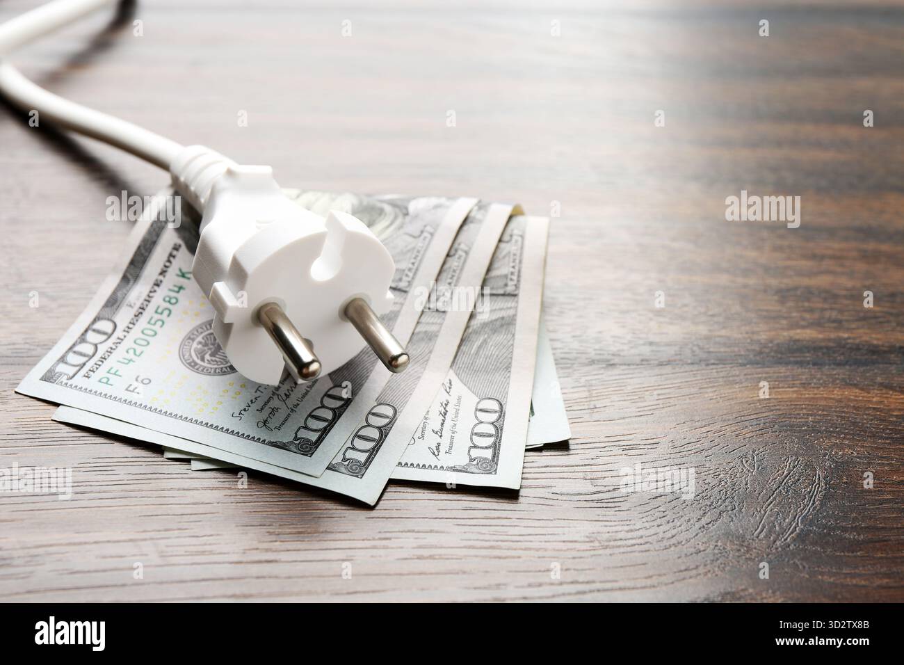 Electrical wire with plug and dollar banknotes on wooden table, closeup ...