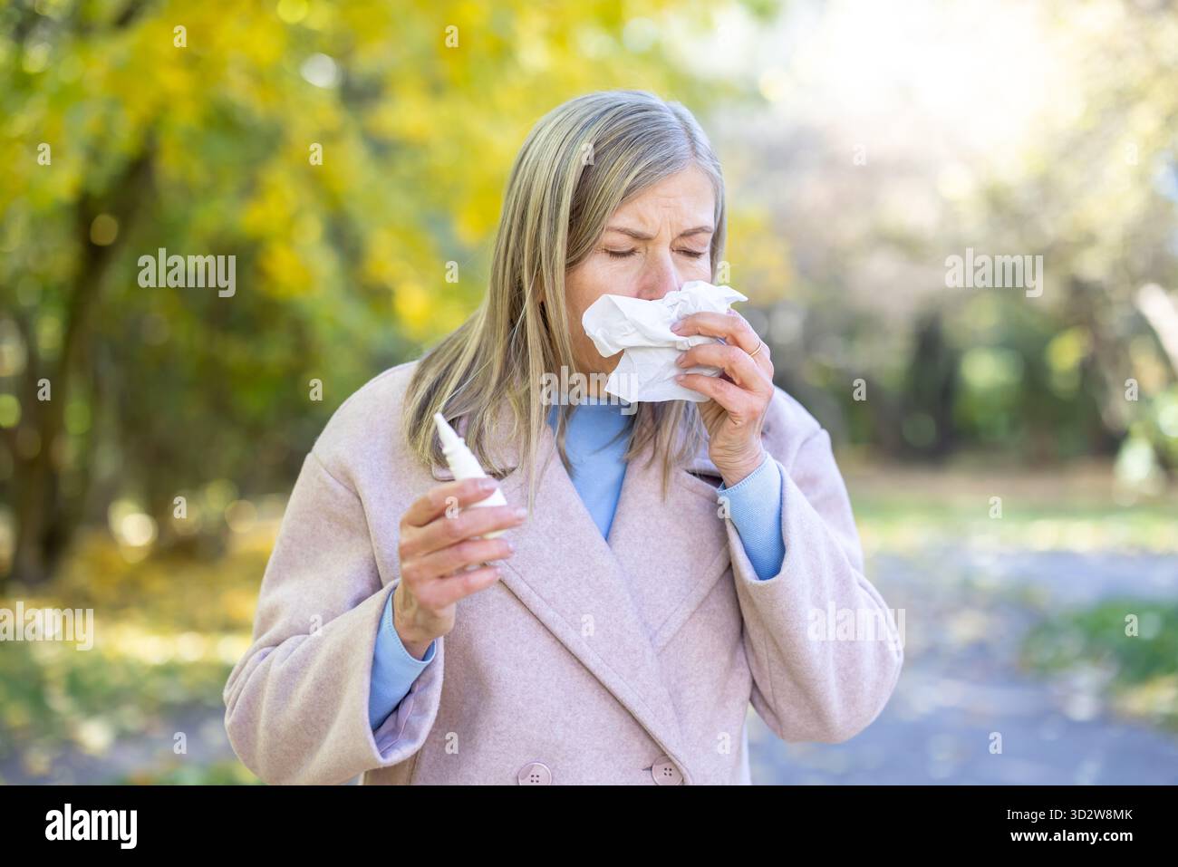 Senior woman with seasonal allergies in autumn park, blowing her nose ...