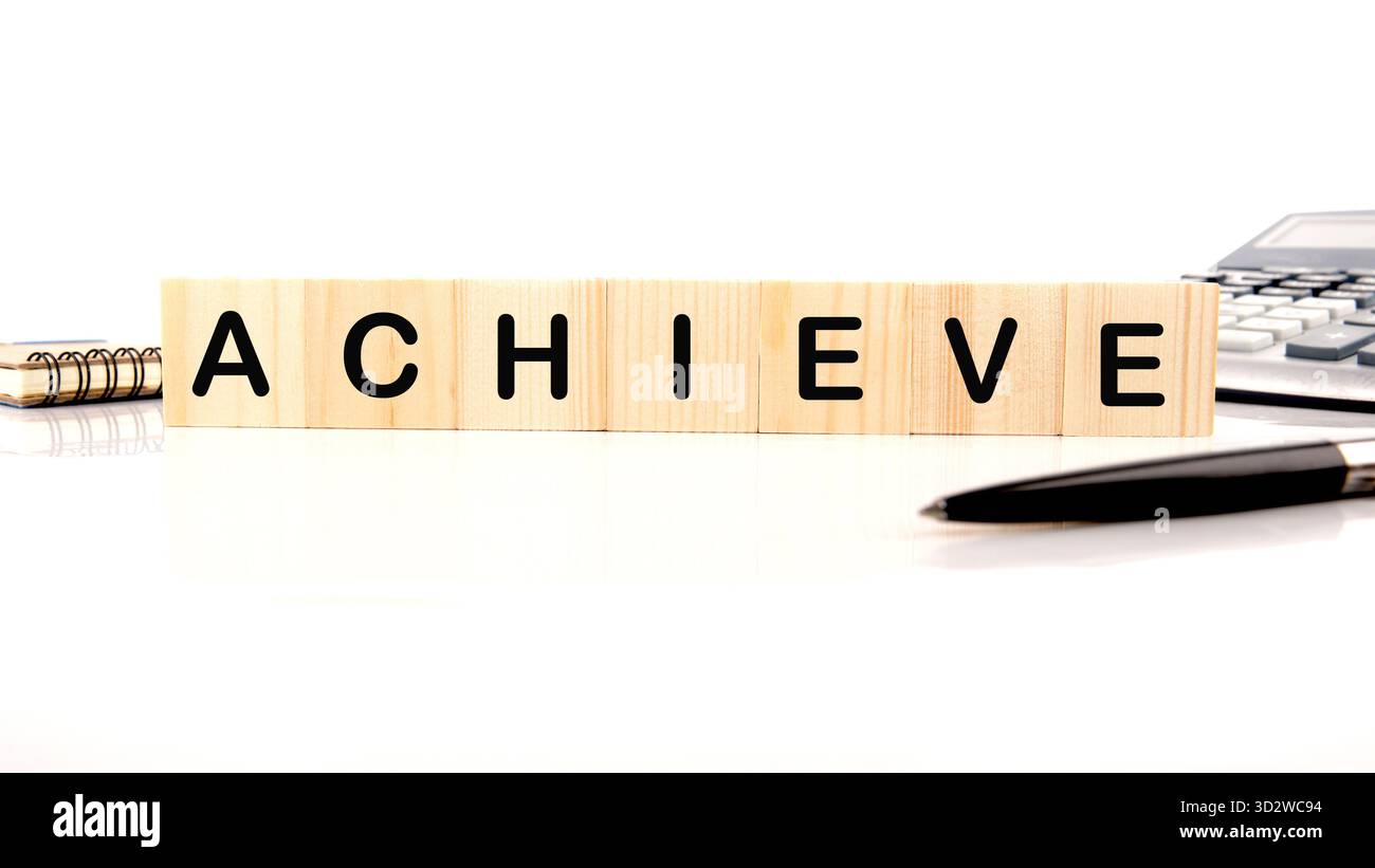 Wooden blocks spell out the word ACHIEVE near a calculator, notebook ...