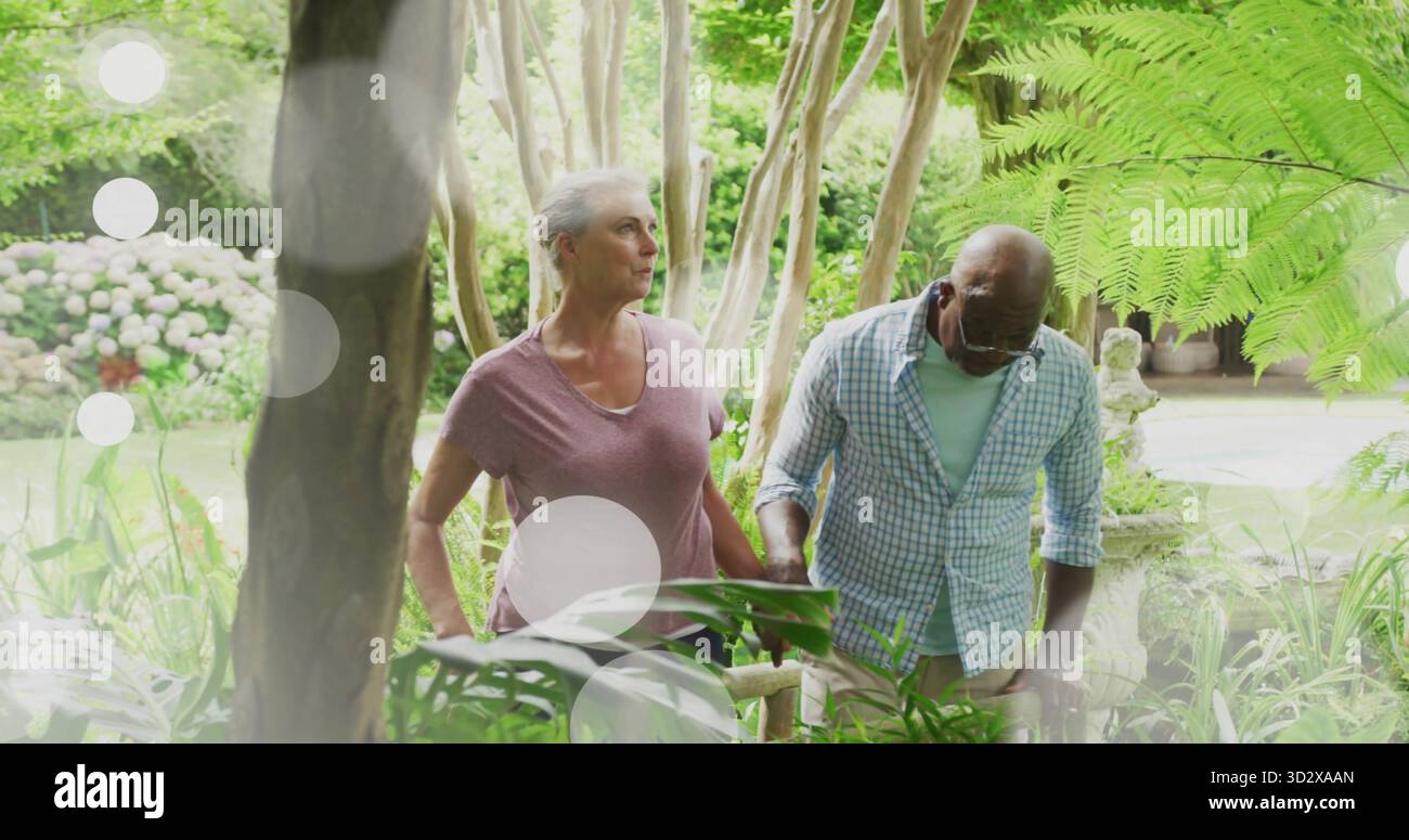 Strolling senior man and mature woman through lush winding garden path ...