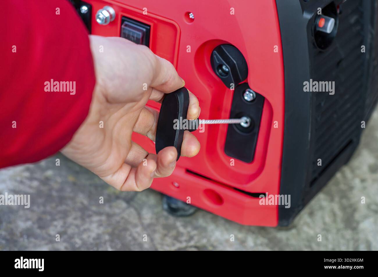 Hand pulling the starter cord of a red portable gasoline generator ...