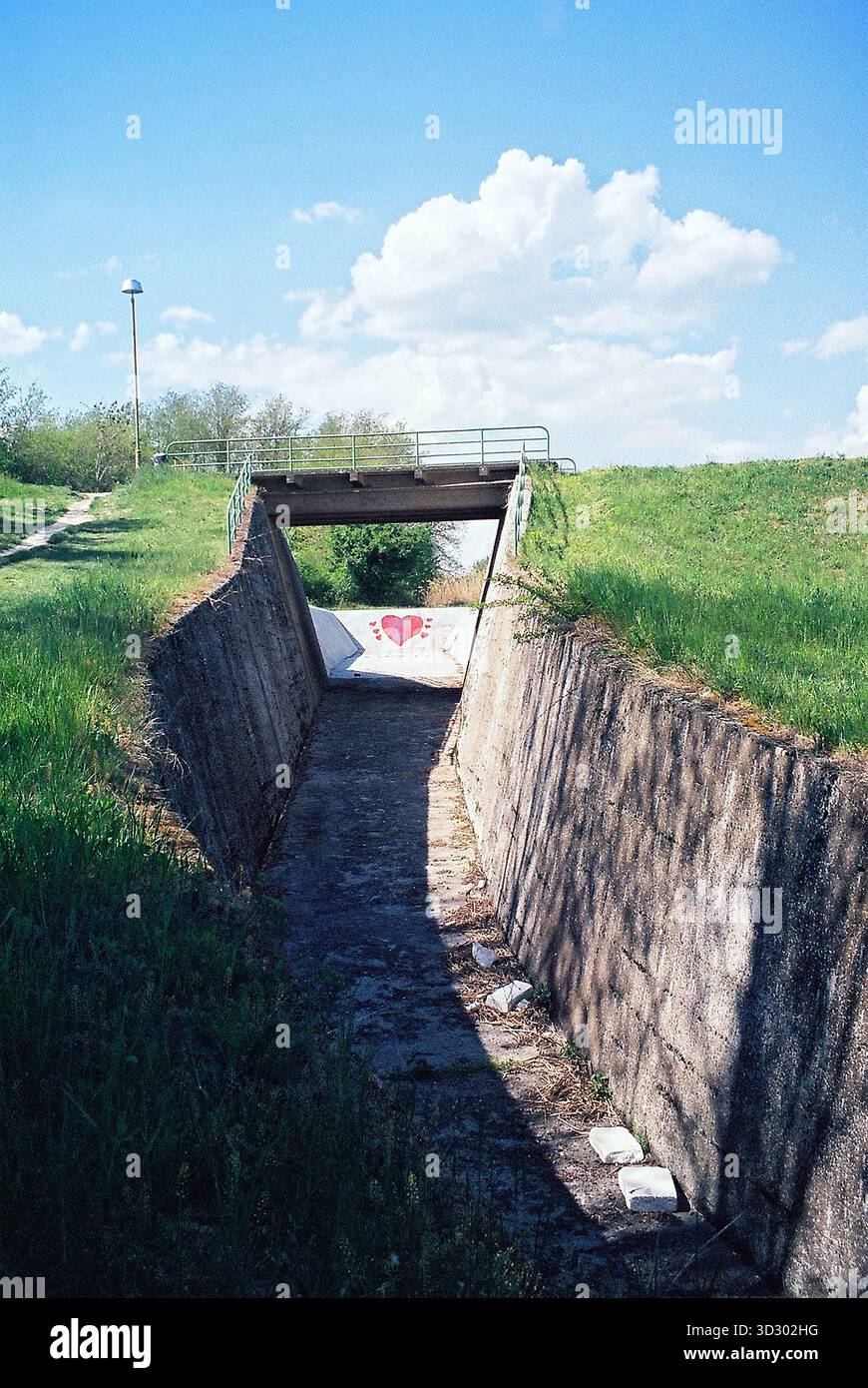 Empty concrete canal passing under a concrete bridge, with a graffiti ...
