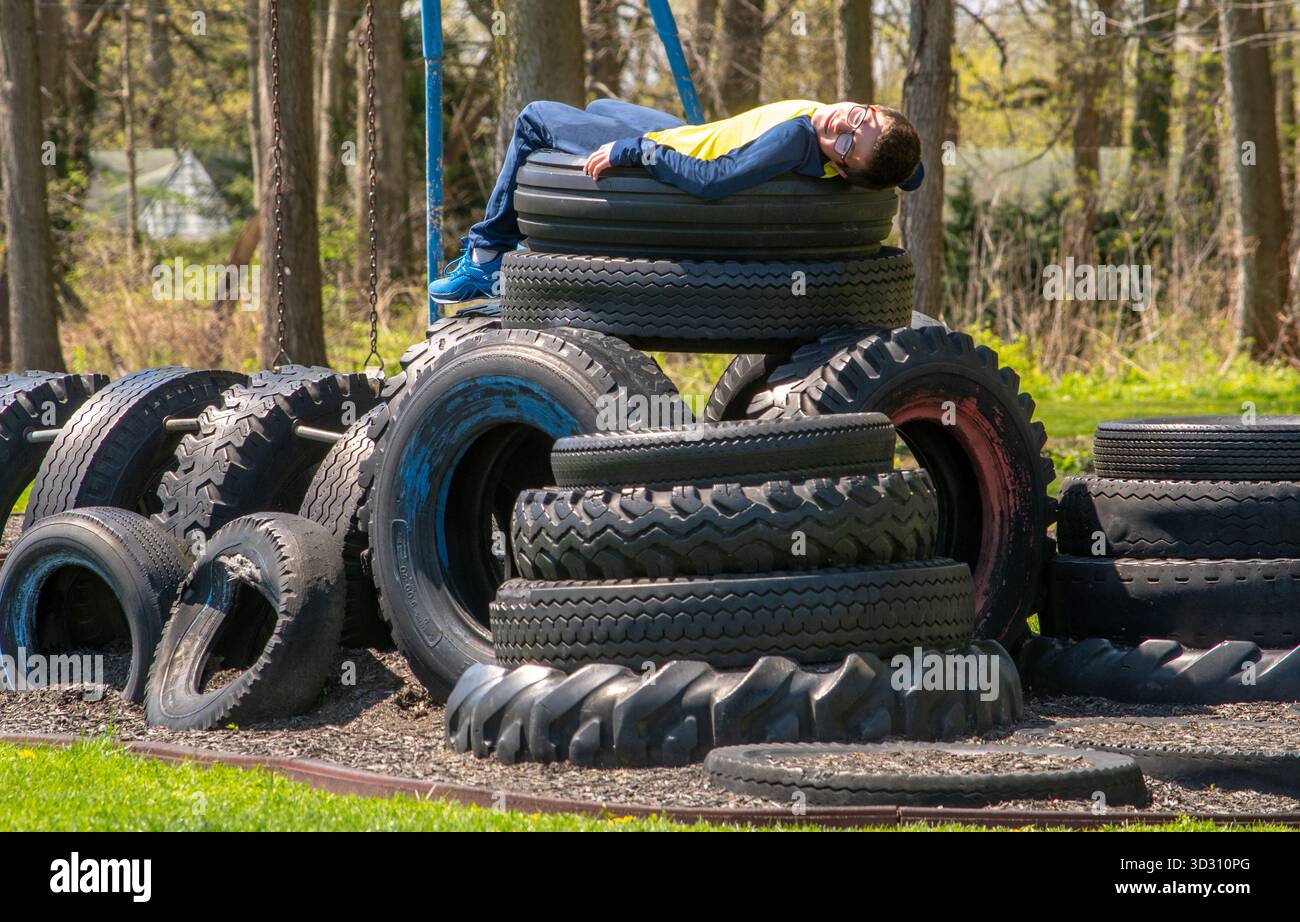 Boy relaxes on the top of a large tire tower in a local playground ...