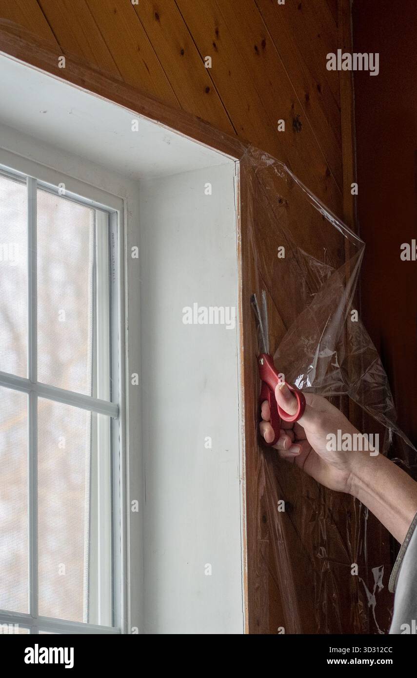 a hand uses a pair of scissors to trim plastic sheets on a insulated ...