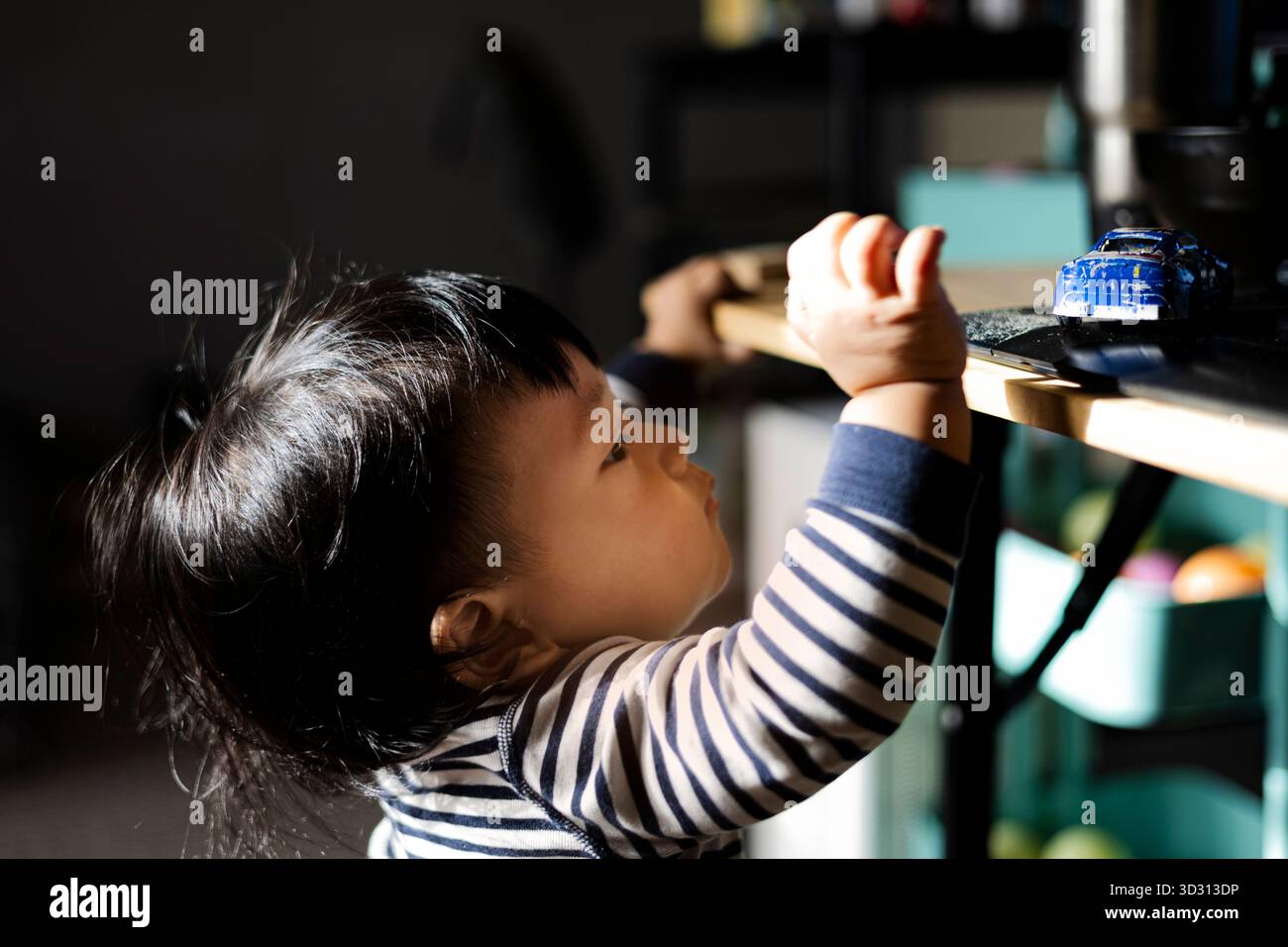 Toddler Standing To Reach Toy On Table, A cute ad photo of a toddler on ...