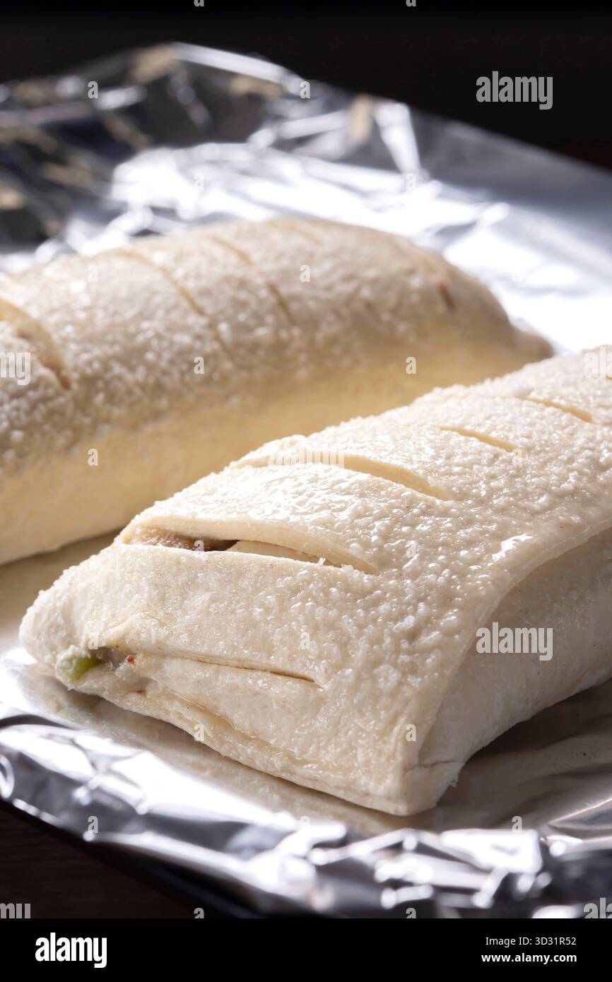 Raw apple strudels, with sliced pastry, on foil ready for cooking in an ...