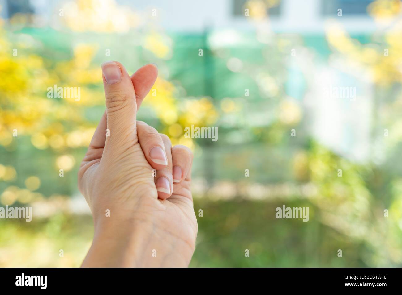 Teenage hand making finger heart gesture outdoors with blurred nature ...