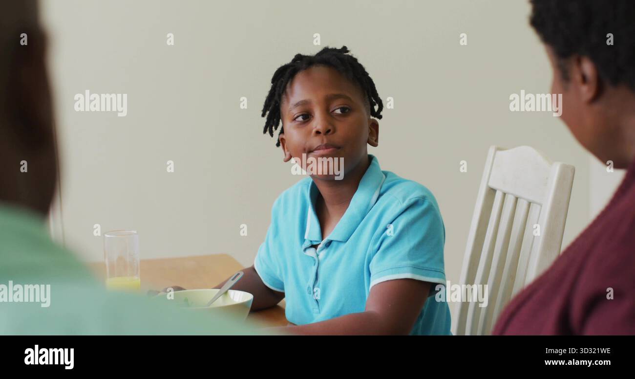 Black boy in polo eating cereal with spoon at dining table, with glass ...