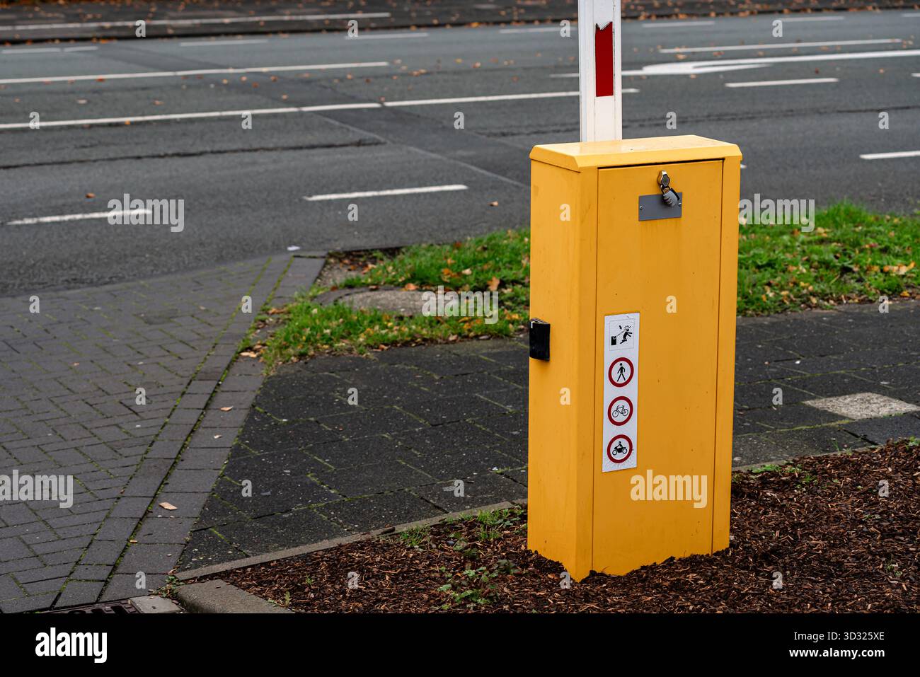 A bright yellow barrier box is positioned next to a paved sidewalk in ...
