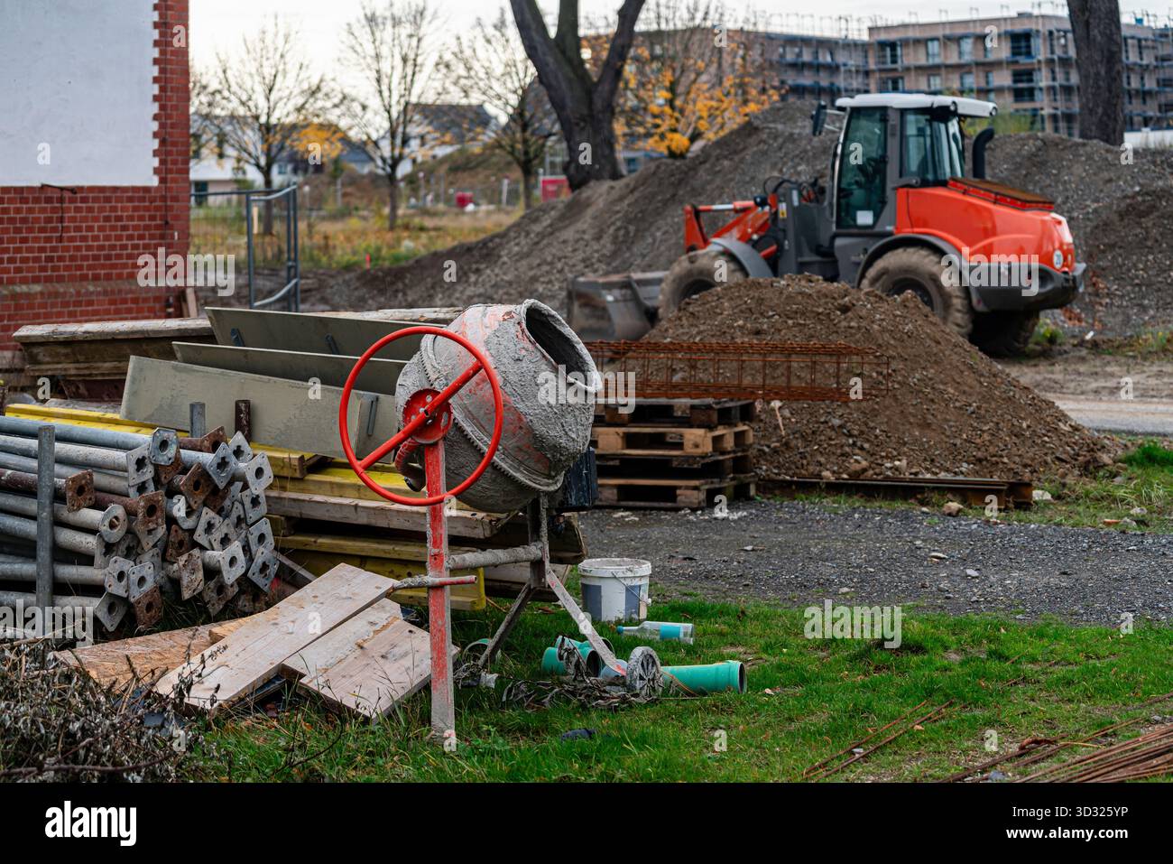 A busy construction site shows a cement mixer and stacks of building ...