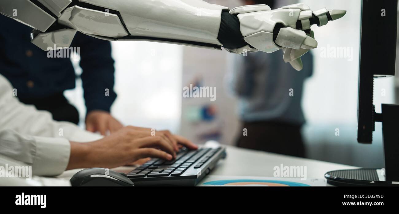 A robotic arm assists a human worker at a keyboard in a modern office ...