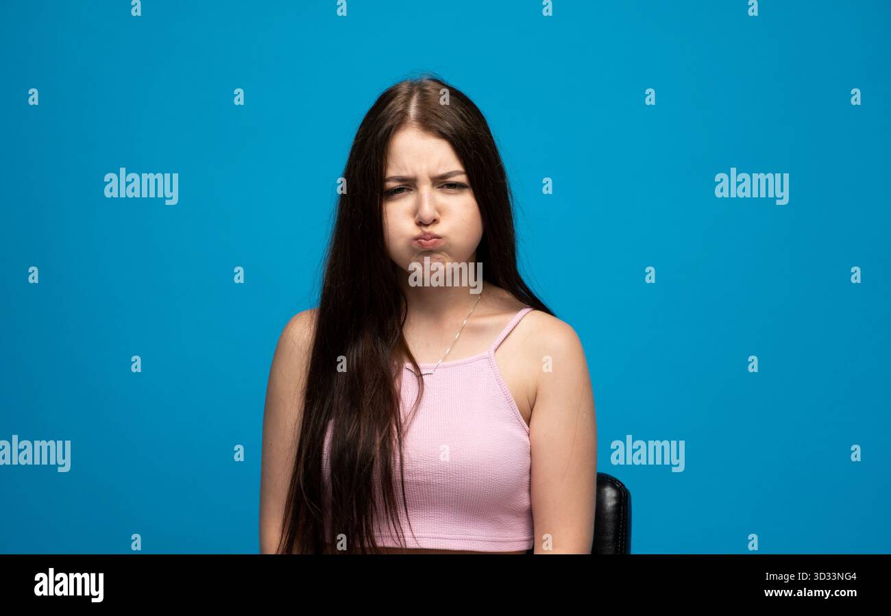 Playful brunette woman with long hair puffing cheeks making funny face ...