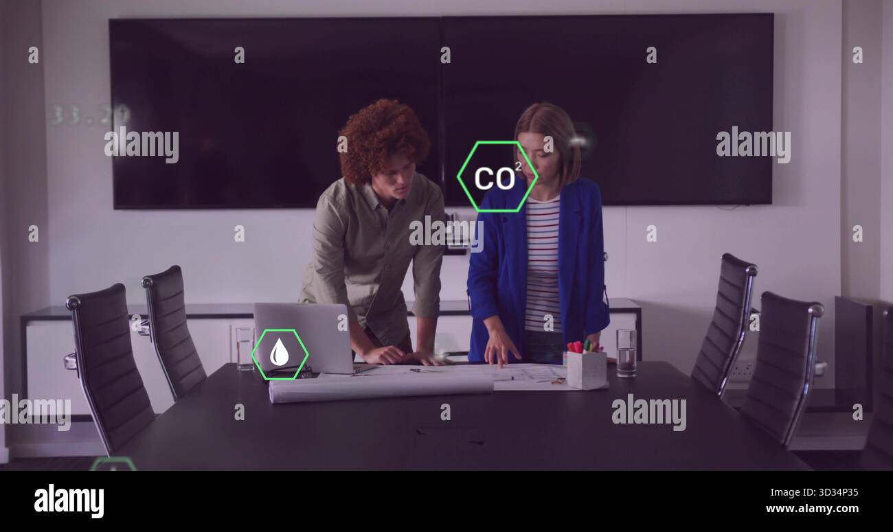 Two colleagues leaning over table in conference room, reviewing plans ...