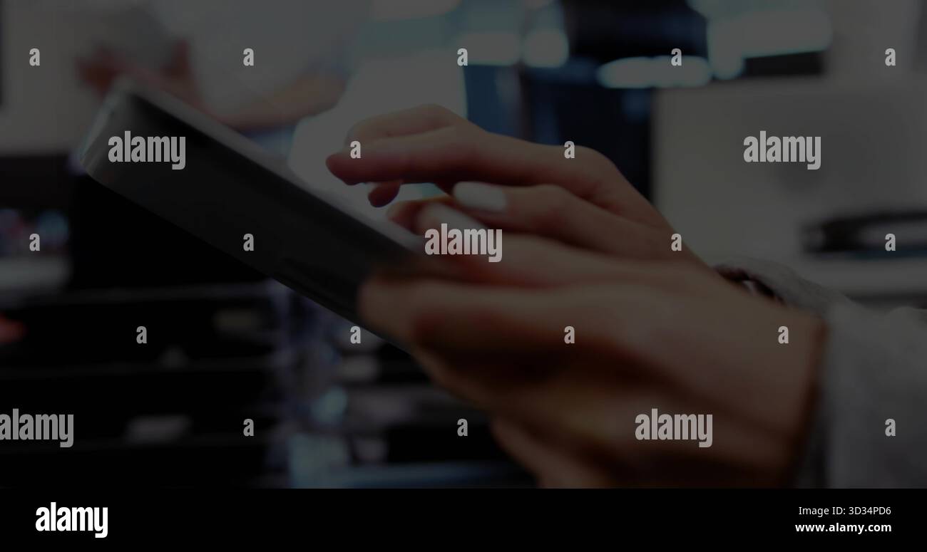 Hands wearing long-sleeve top tapping touchscreen tablet at office desk ...