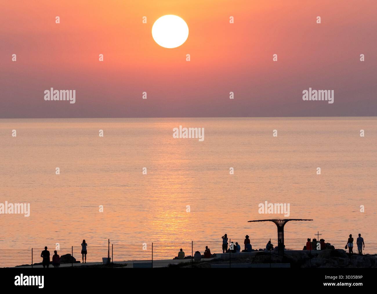 Tourists watch the sun setting from the coastal path, Paphos, Cyprus ...