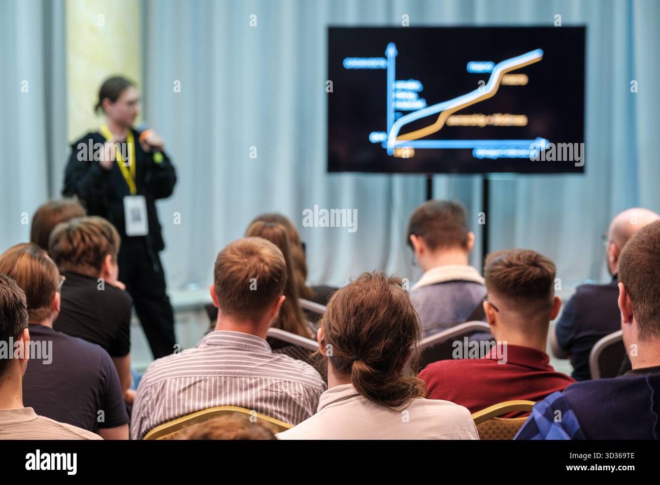 Speaker presents data to seated audience in conference room with large ...